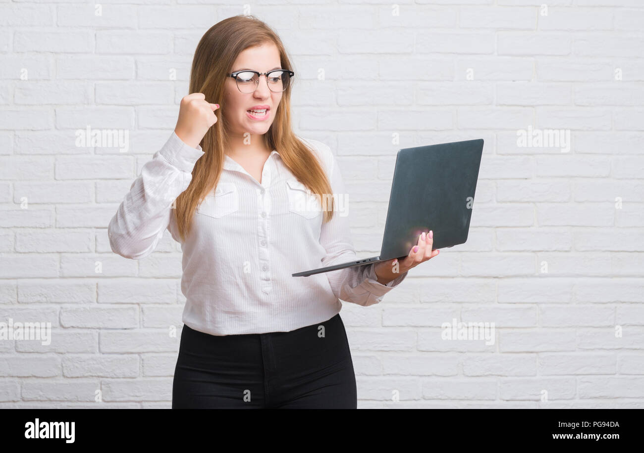Young adult business woman over white brick wall holding computer ...