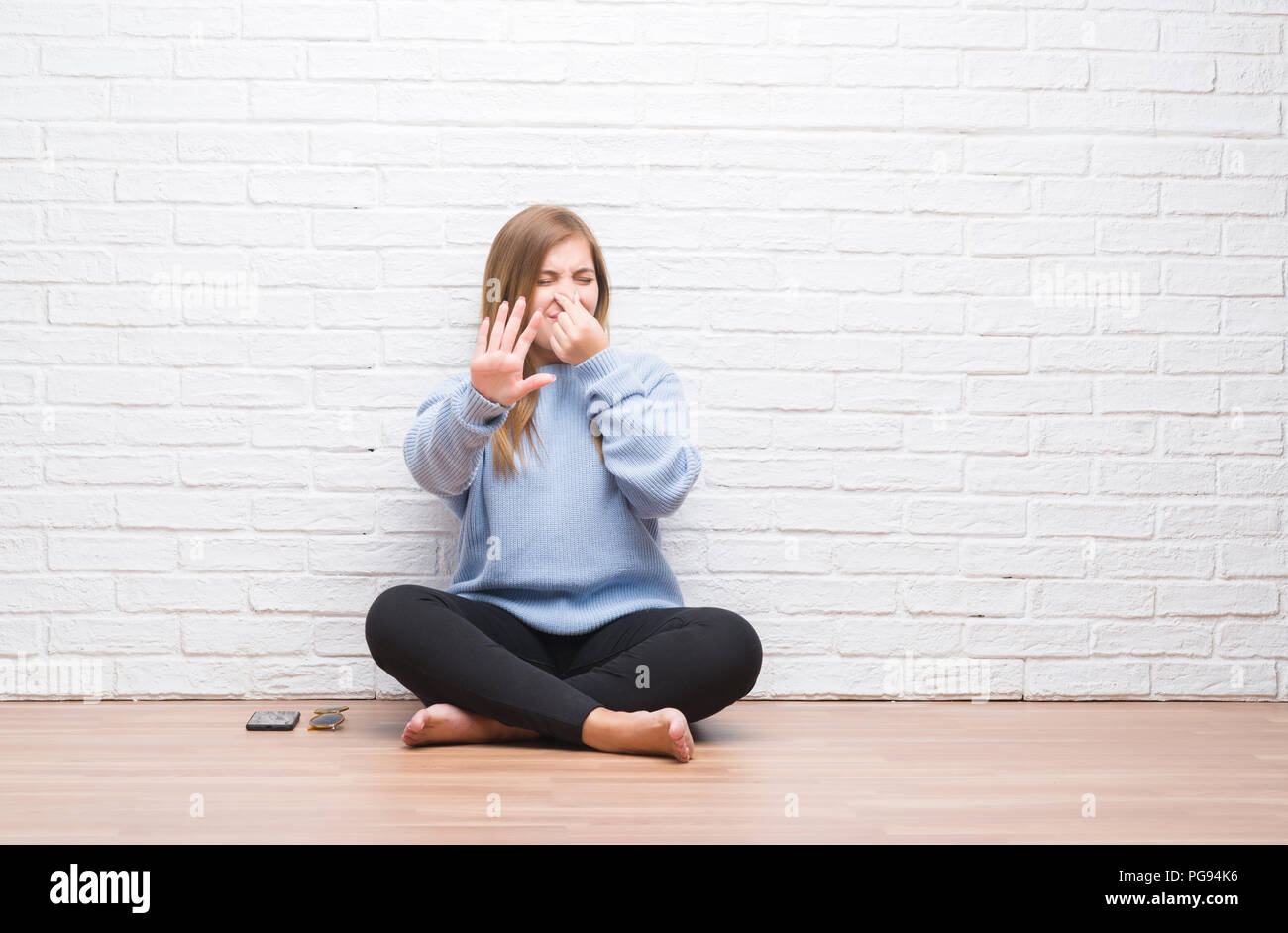 Young adult woman sitting on the floor in autumn over white brick wall ...