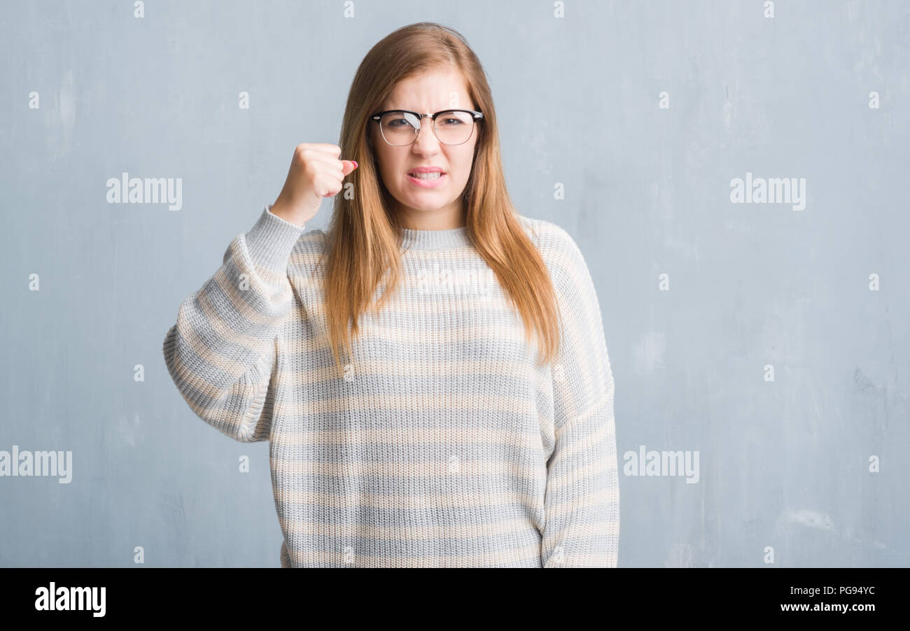 Young adult woman over grey grunge wall wearing glasses annoyed and ...
