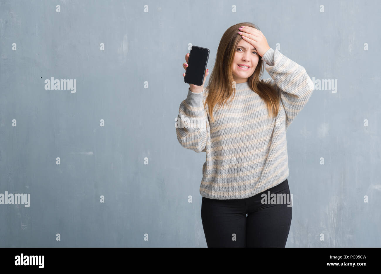 Young adult woman over grey grunge wall showing blank screen of ...