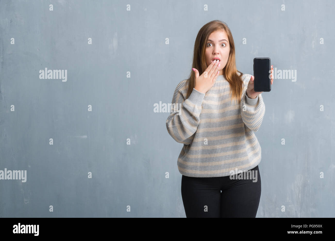 Young adult woman over grey grunge wall showing blank screen of ...