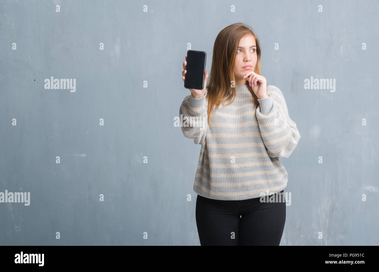 Young adult woman over grey grunge wall showing blank screen of ...