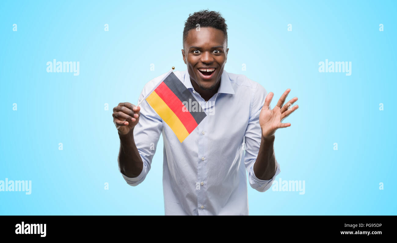 Young african american man holding german flag very happy and excited ...