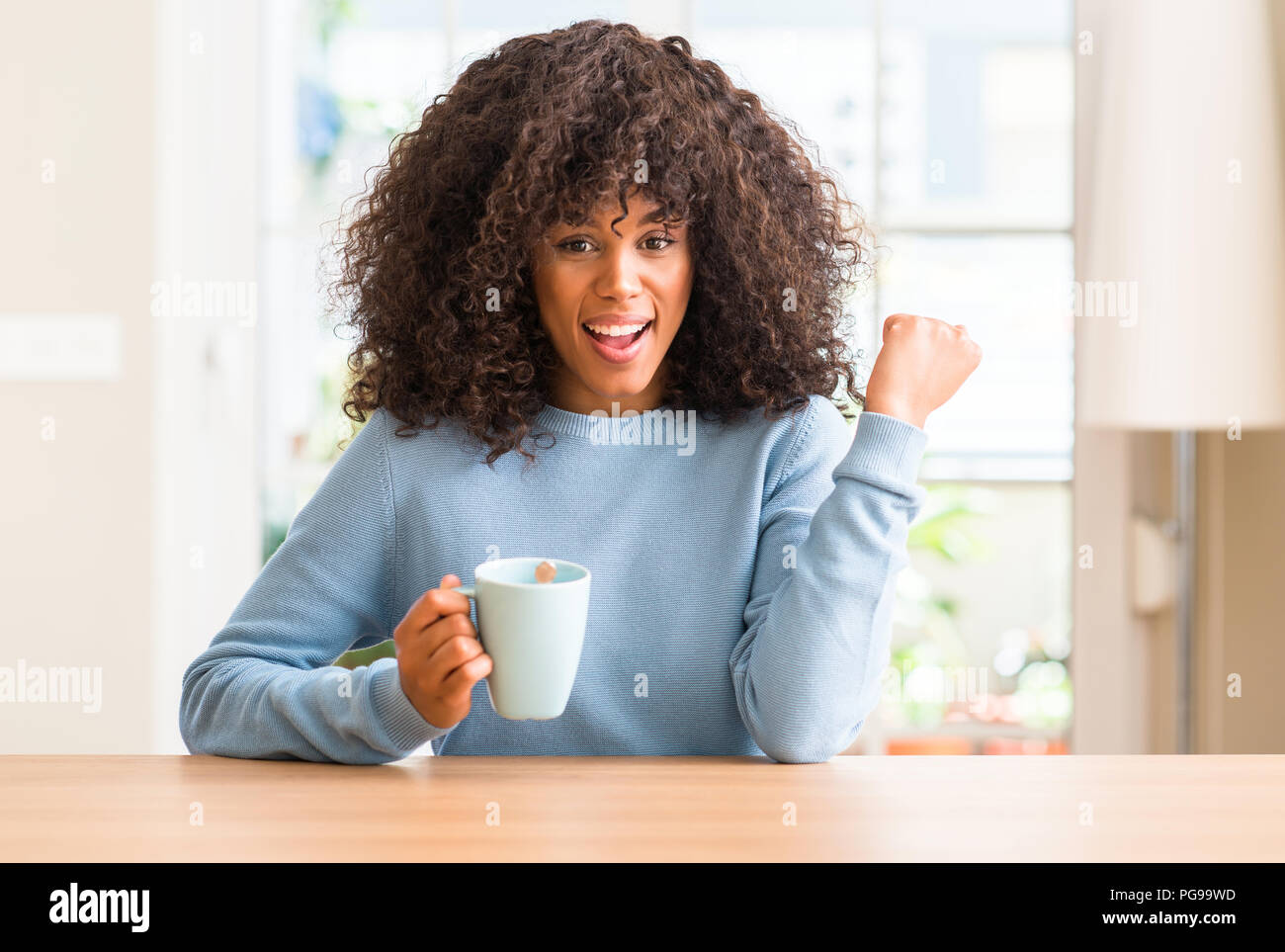 African american woman holding a cup of coffee at home screaming proud ...