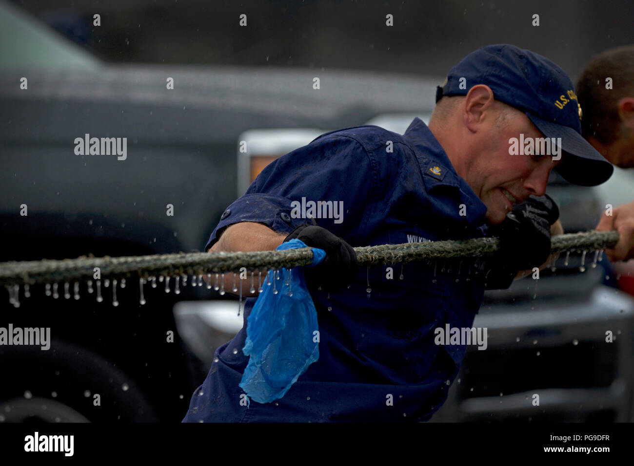 A Coast Guard chief petty officer drenched from the pouring rain, pulls ...