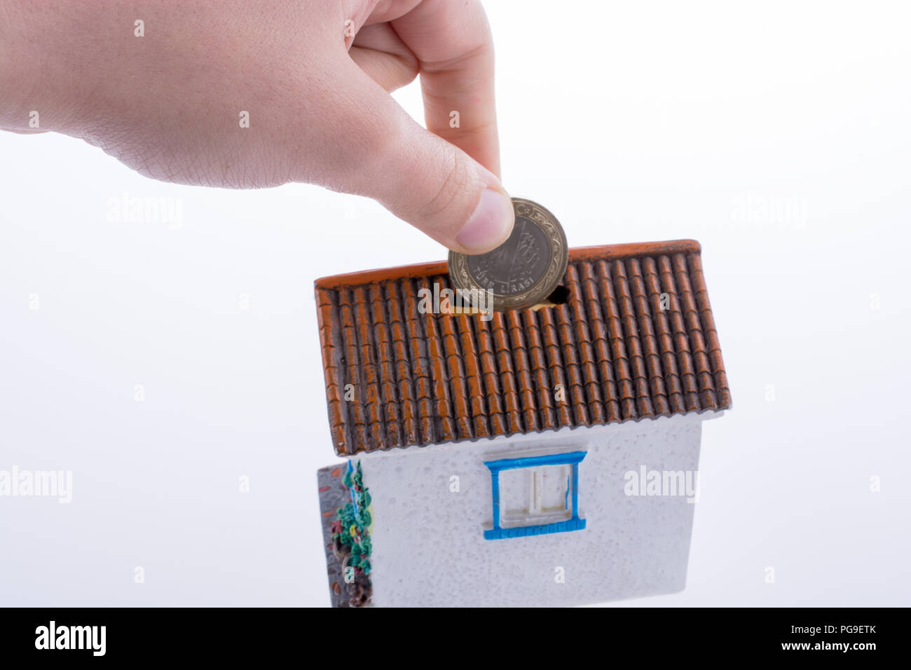Hand dropping coin into the moneybox in the shape of a model house ...
