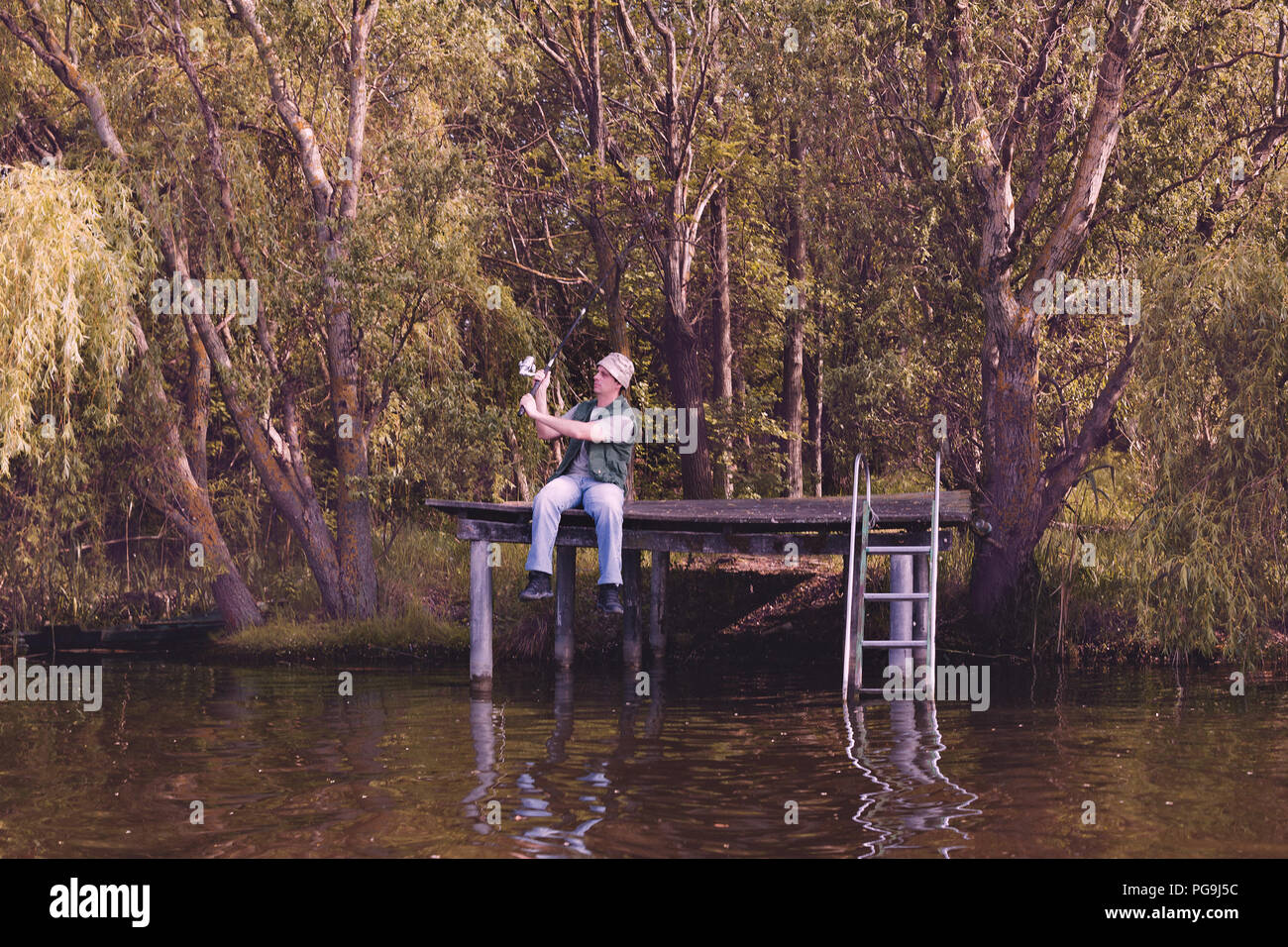 Fisherman with fishing rod catching fish on river bank Stock Photo - Alamy