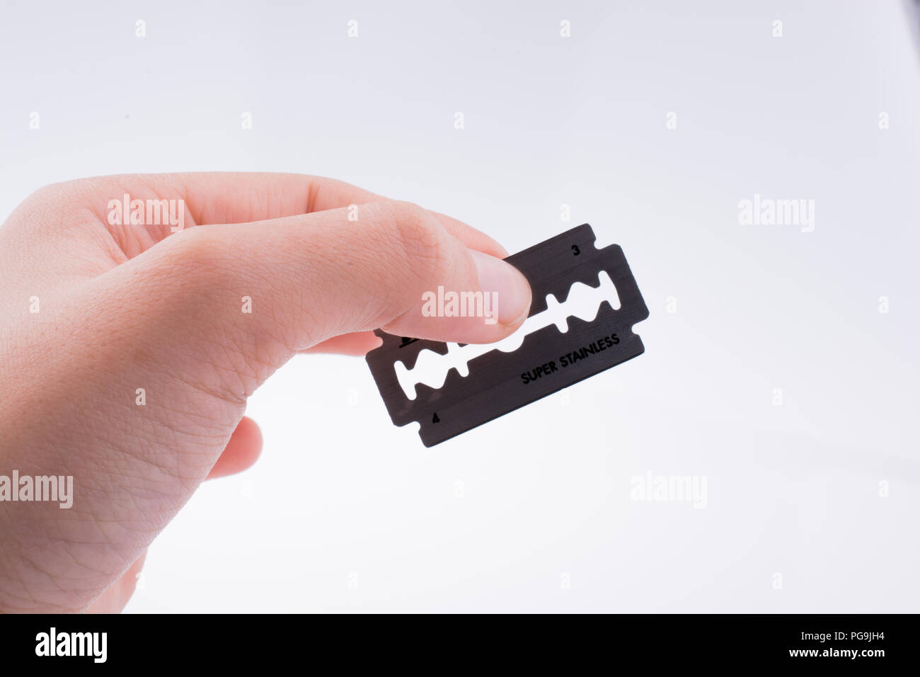 Hand holding a razor blade on a white background Stock Photo - Alamy