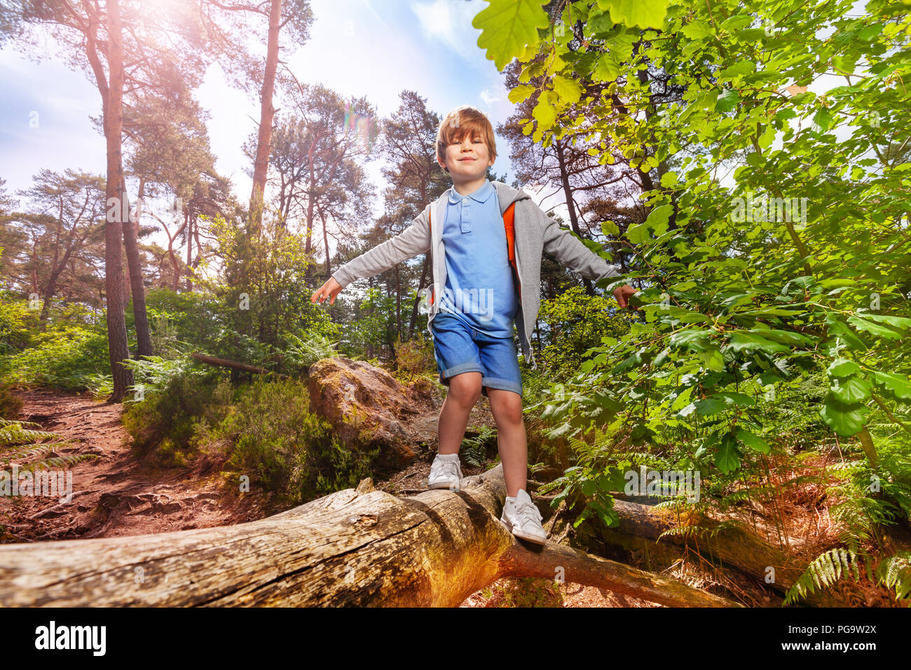 Small boy walks over log in forest with backpack Stock Photo - Alamy