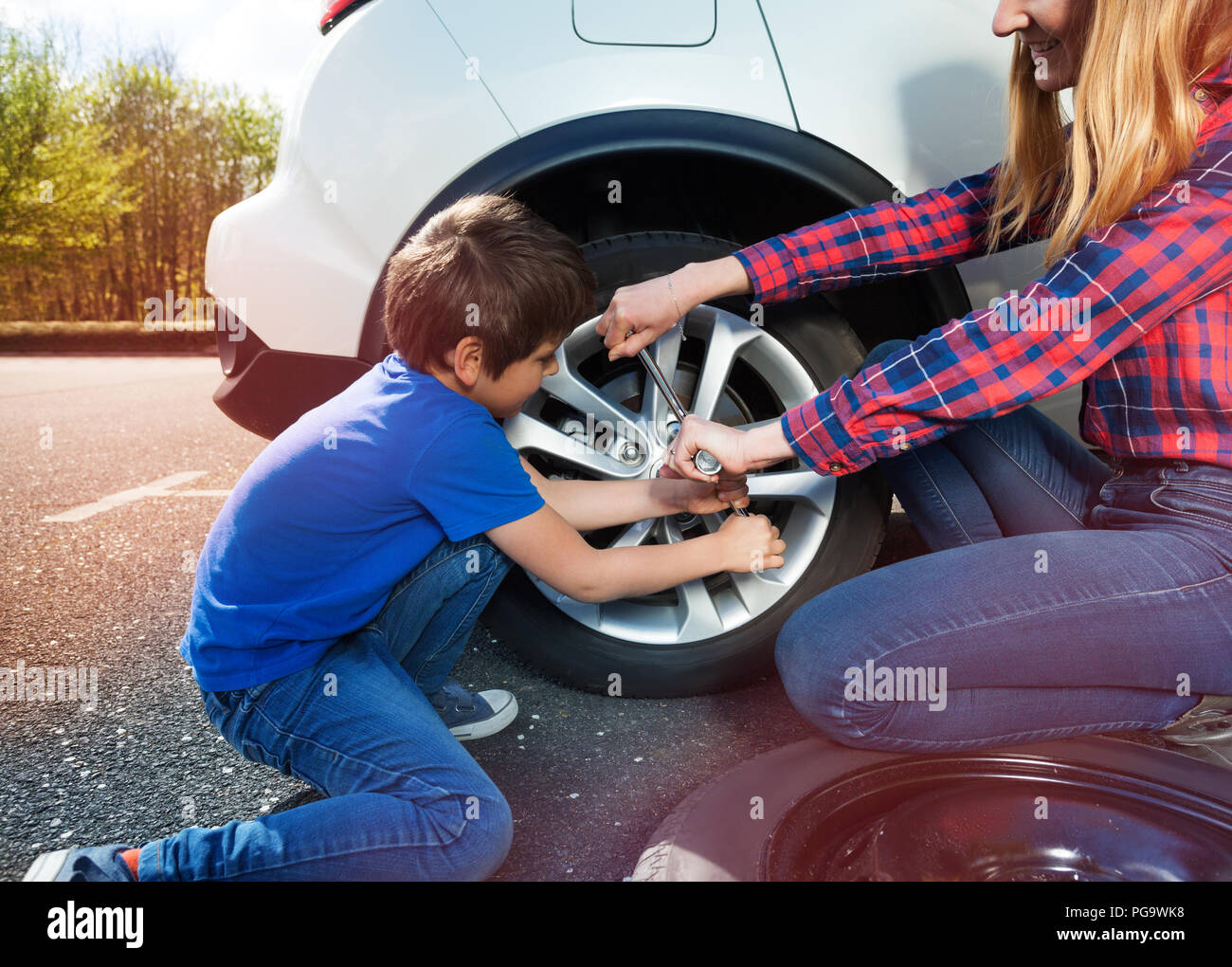 Boy helping mother to change tyre using lug wrench Stock Photo - Alamy