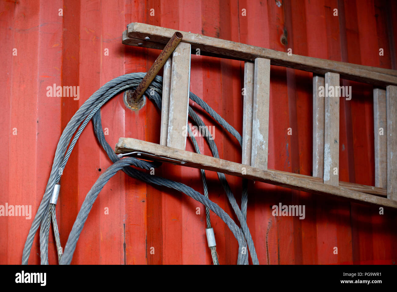 A wooden ladder and a steel rope hanging from a red metal wall Stock ...