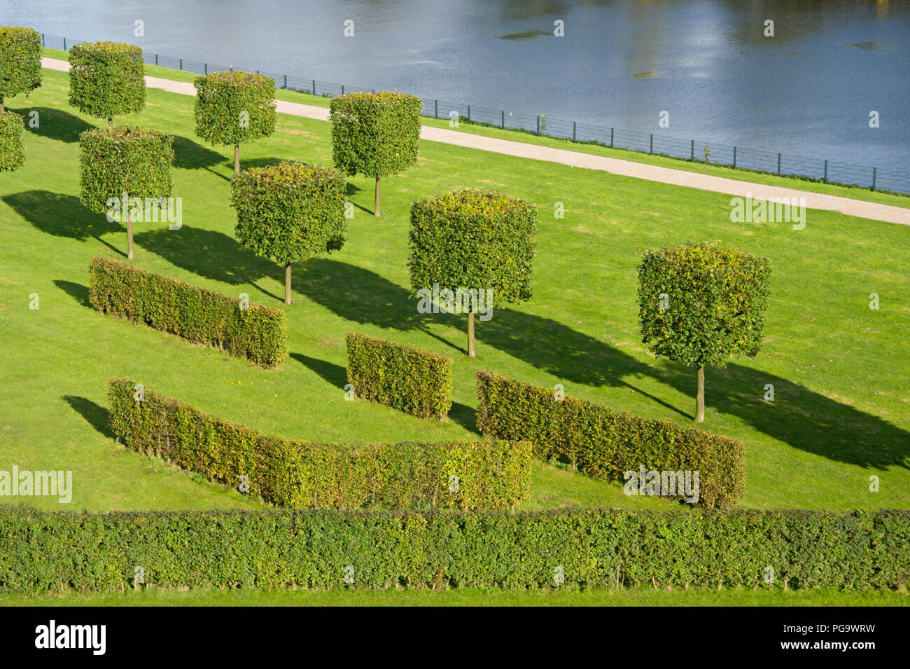Interesting garden architecture with cubic trees in a park by a canal ...