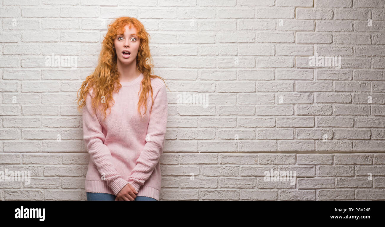Young Redhead Woman Standing Over Brick Wall Afraid And Shocked With