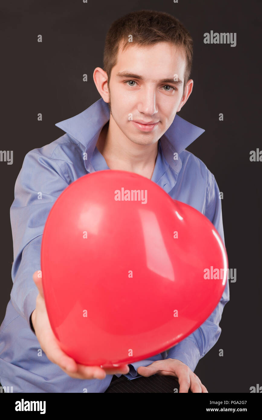 Young guy holding a red heart-shaped balloon Stock Photo - Alamy
