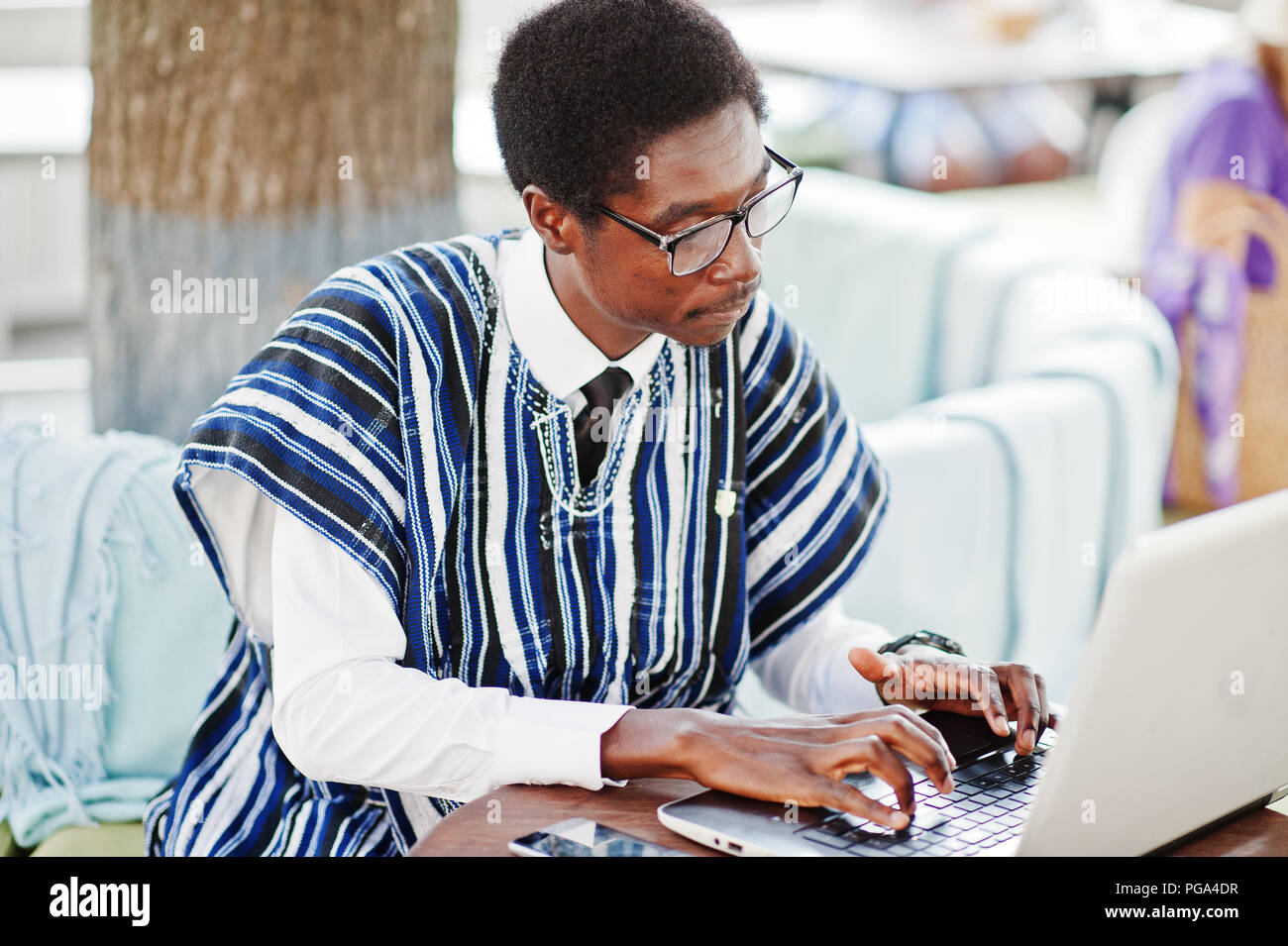 African man in traditional clothes and glasses sitting behind laptop at ... African man in traditional clothes and glasses sitting behind laptop at ...