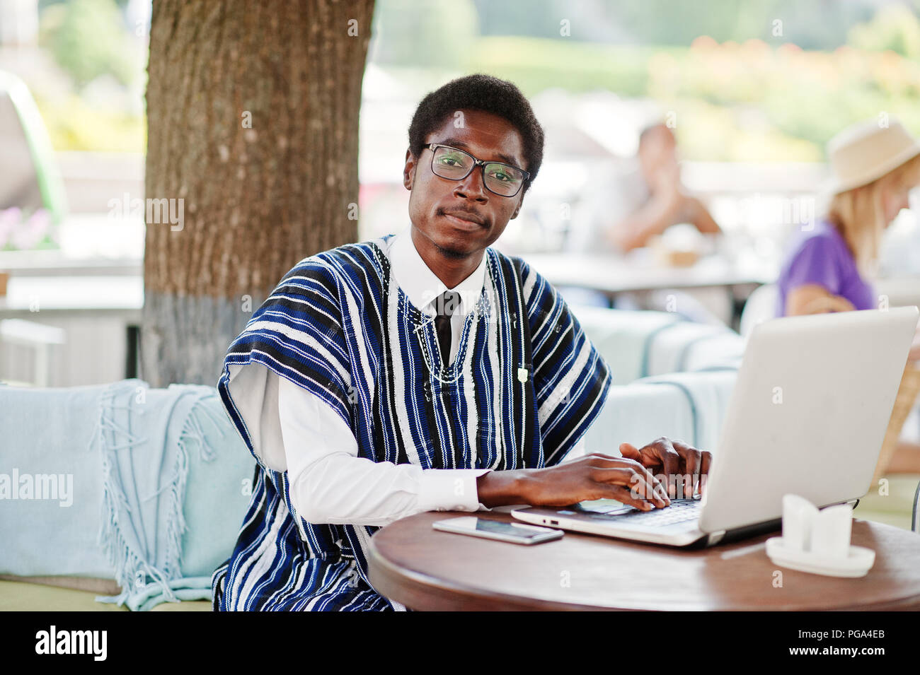 African man in traditional clothes and glasses sitting behind laptop at ...