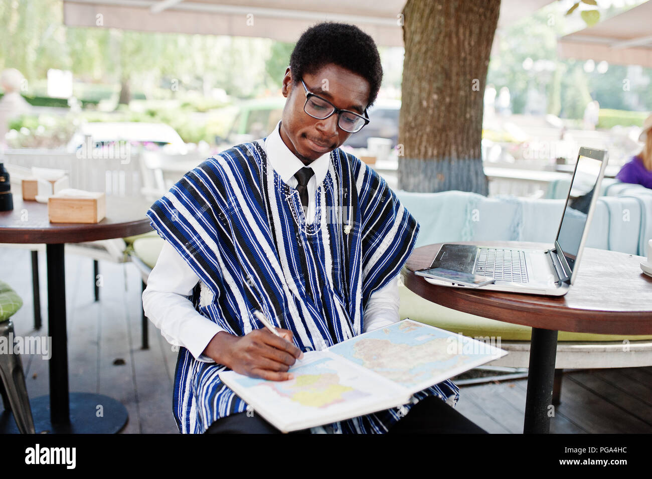 African man in traditional clothes and glasses sitting behind laptop at ...