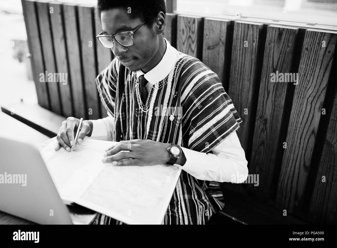 African man in traditional clothes and glasses sitting behind laptop at ...