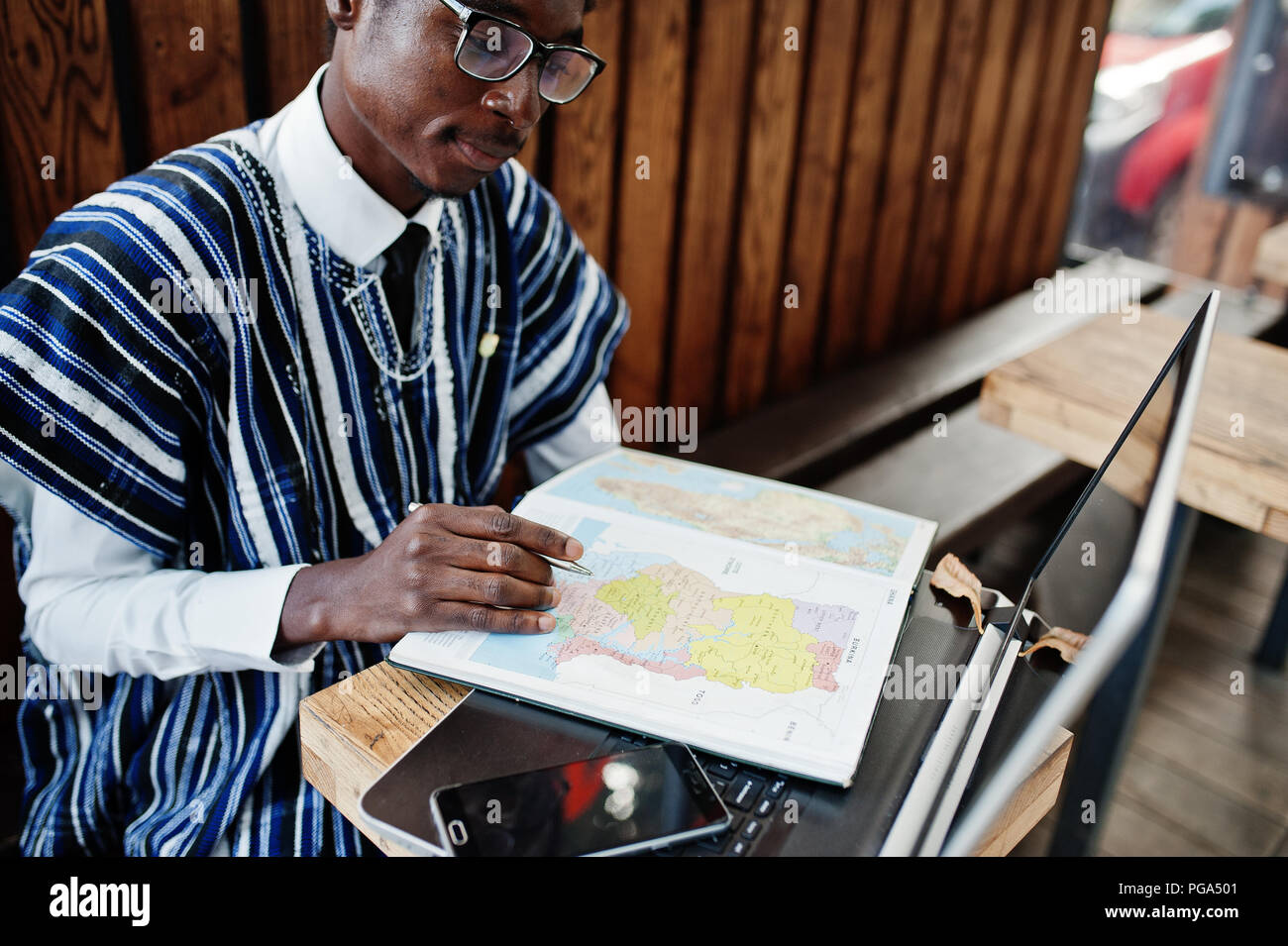 African man in traditional clothes and glasses sitting behind laptop at ...