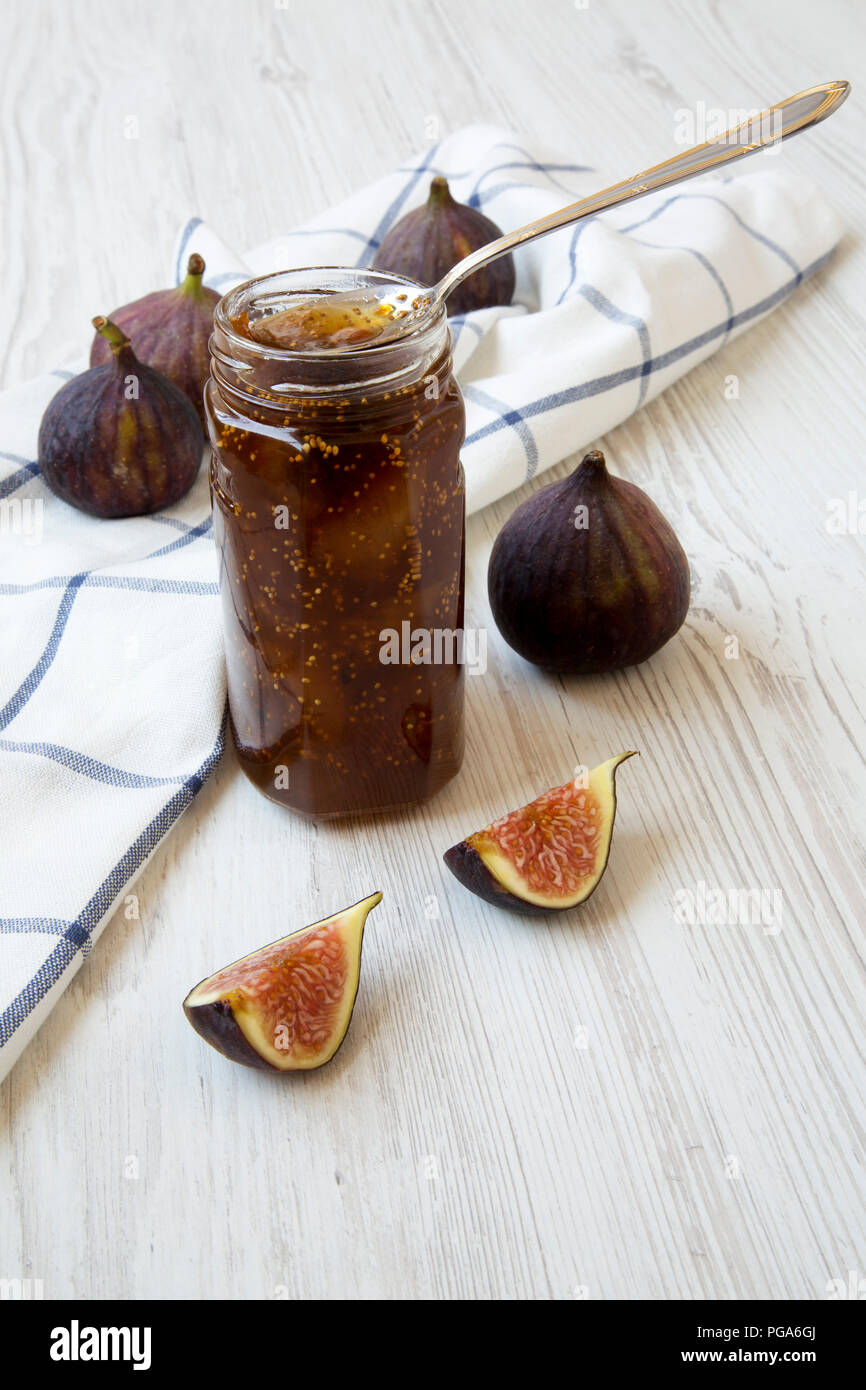 Fig jam in glass jar and fresh figs on white wooden background, side ...