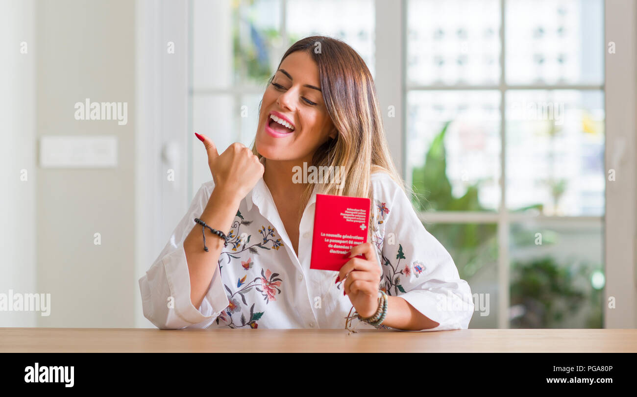 Young woman at home holding a passport of Switzerland pointing with ...