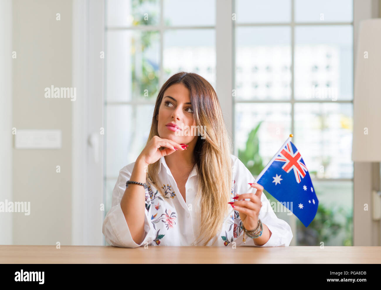 Young woman at home holding flag of Australia serious face thinking ...