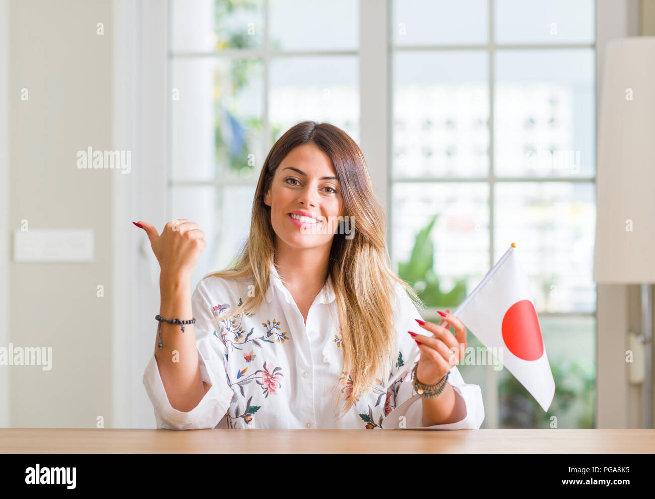 Young woman at home holding flag of Japan pointing with hand and finger ...