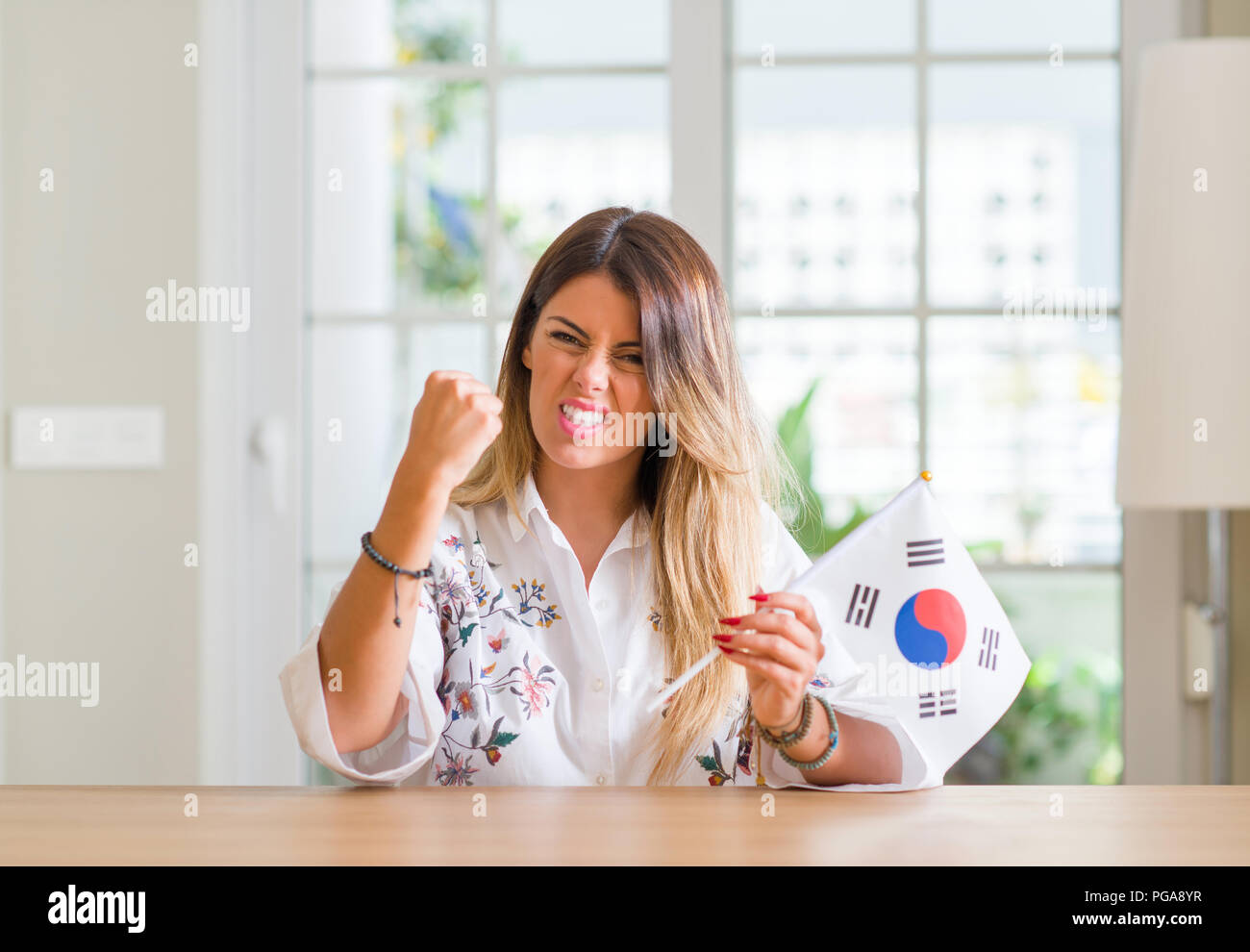 Young woman at home holding flag of South Korea annoyed and frustrated ...