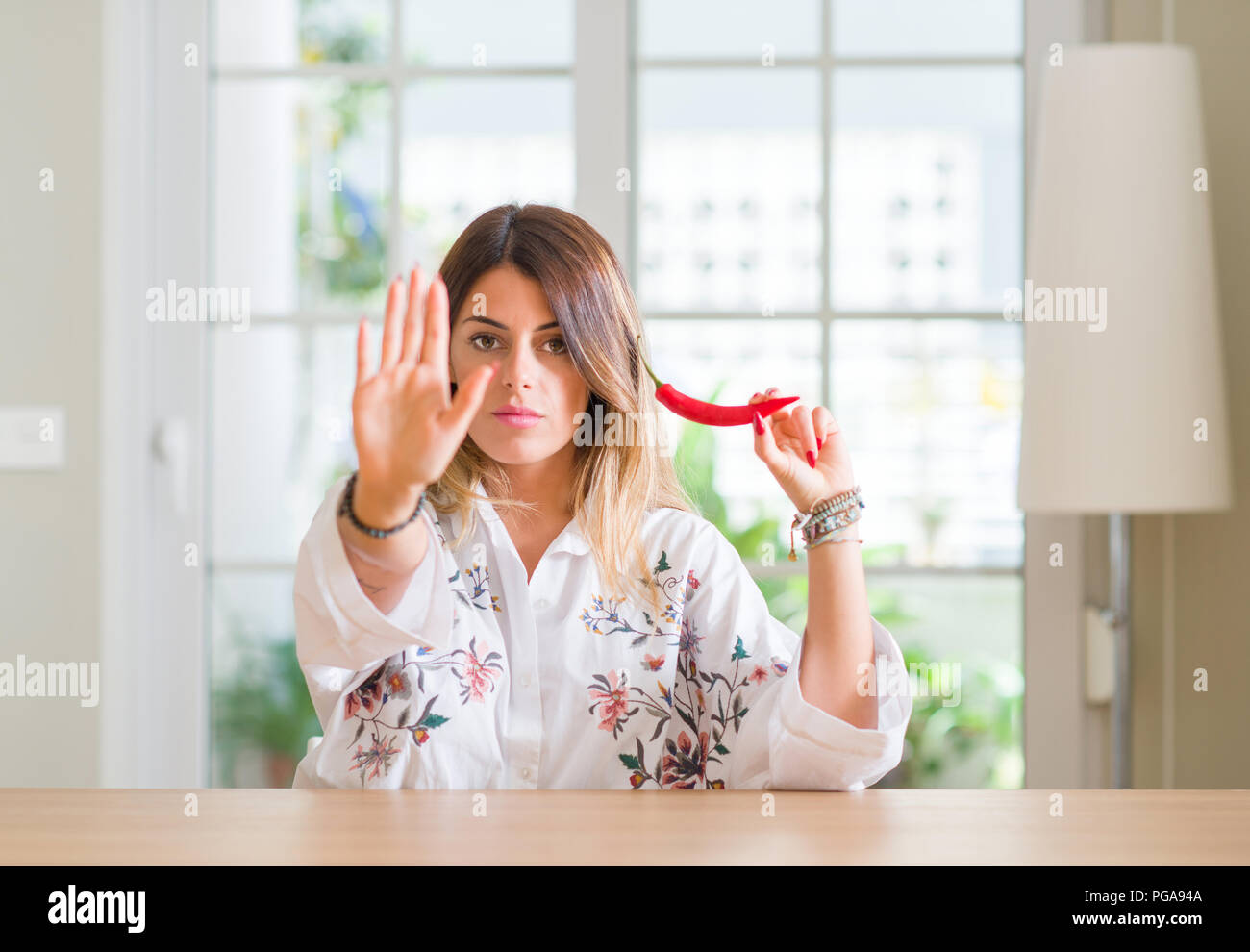 Young woman at home eating red hot chili pepper with open hand doing ...