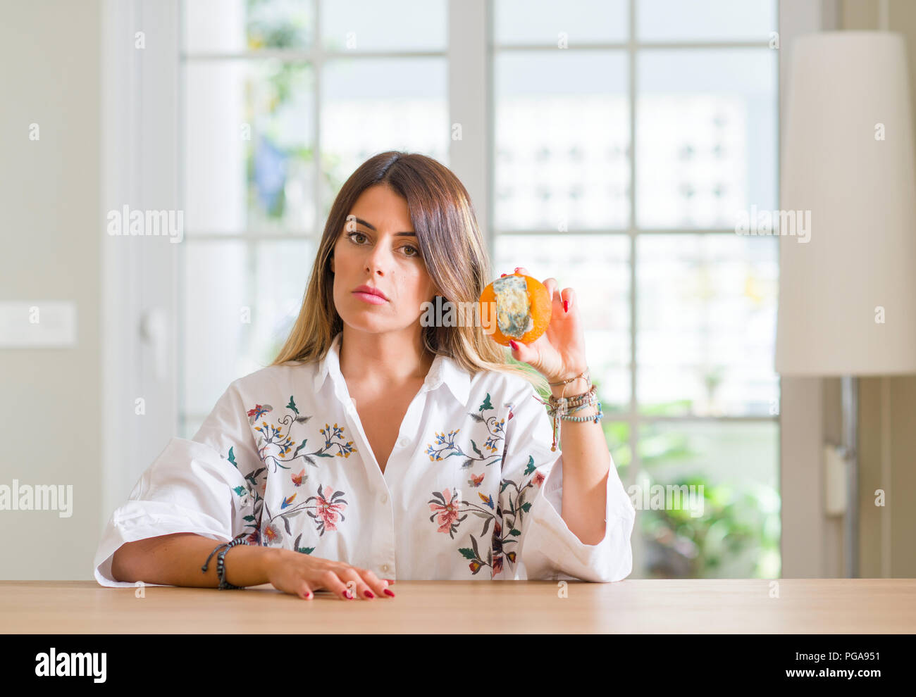 Young woman at home holding rotten orange with a confident expression ...
