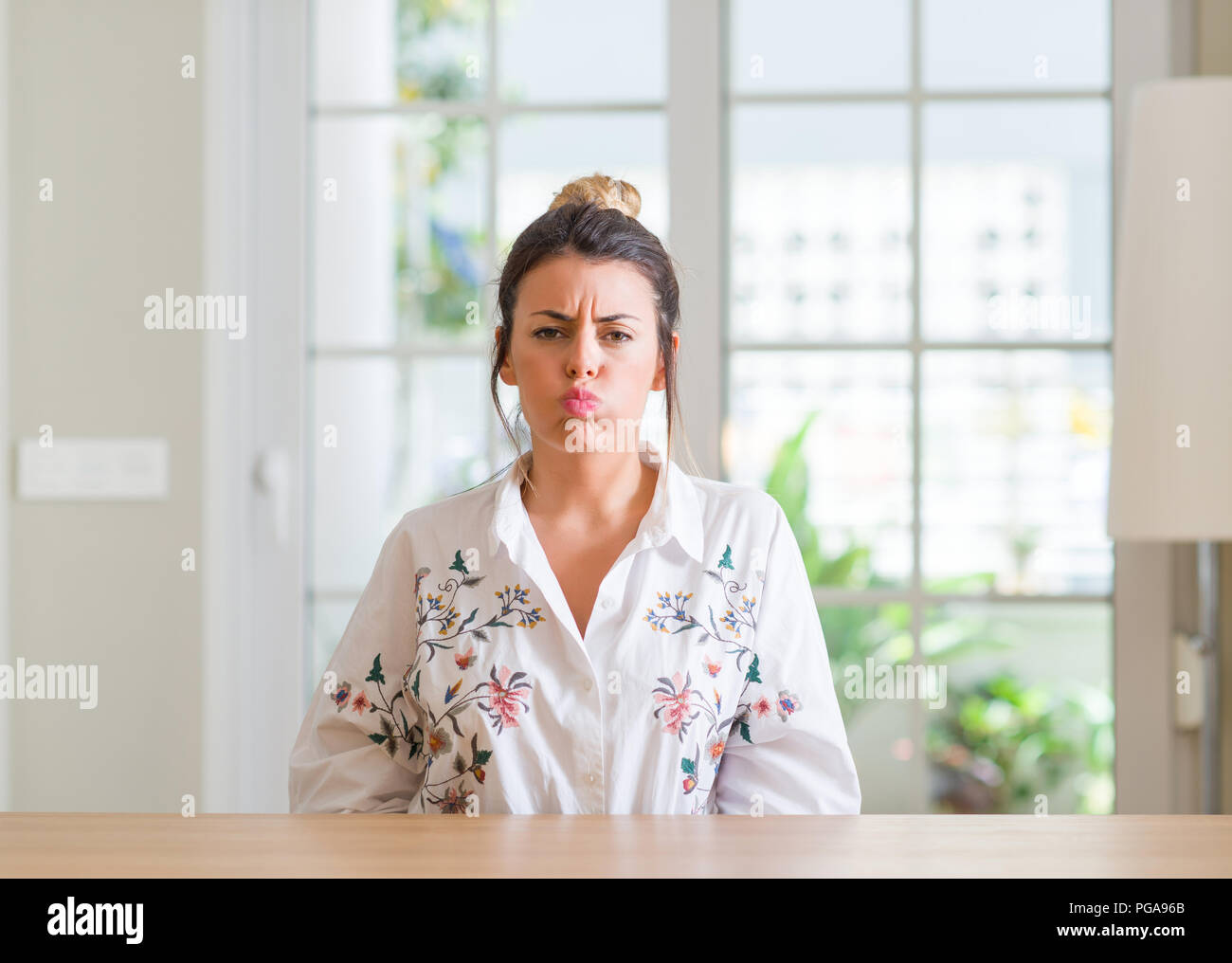 Young woman at home puffing cheeks with funny face. Mouth inflated with ...