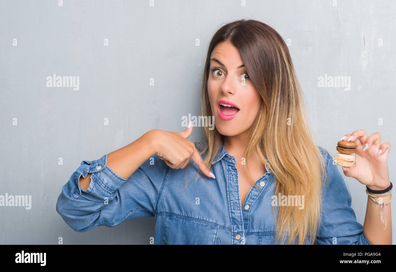 Young adult woman over grey grunge wall eating chocolate macarons with ...