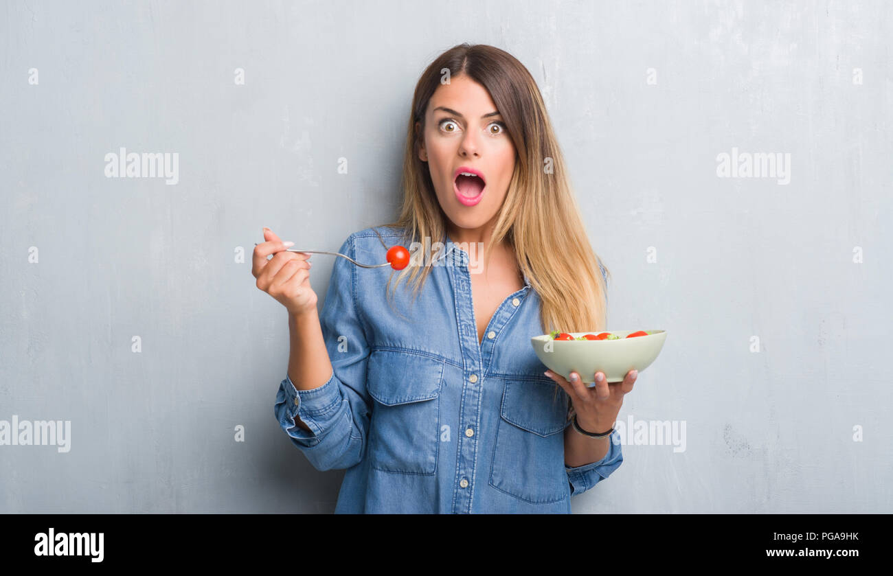 Young adult woman over grey grunge wall eating healthy tomato salad ...