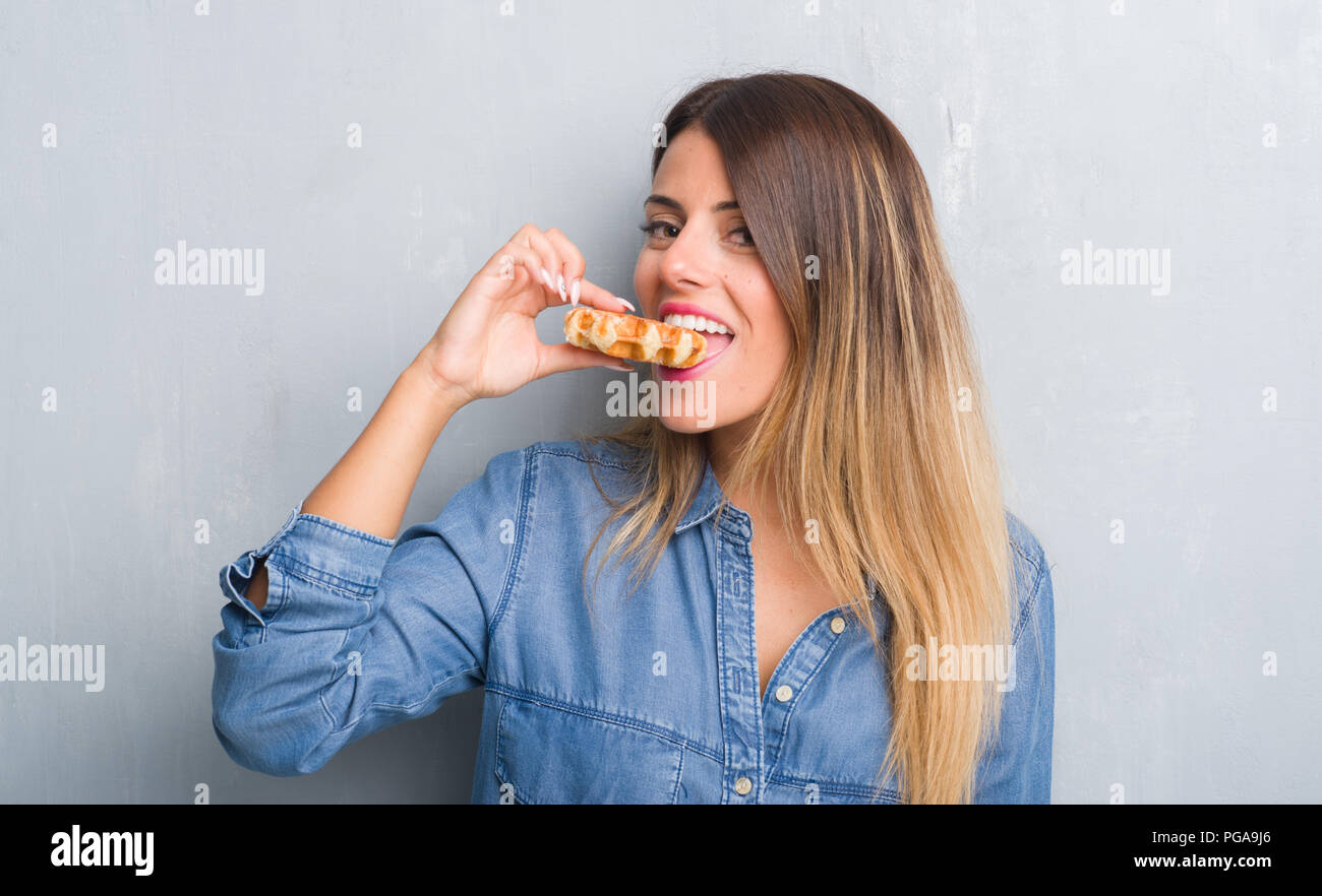 Young adult woman over grey grunge wall eating Belgium waffle with a ...