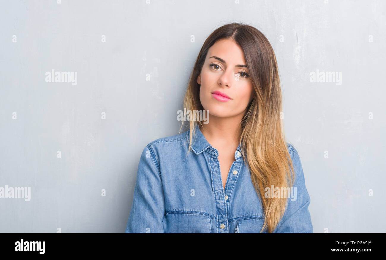 Young adult woman over grey grunge wall wearing denim outfit with a ...