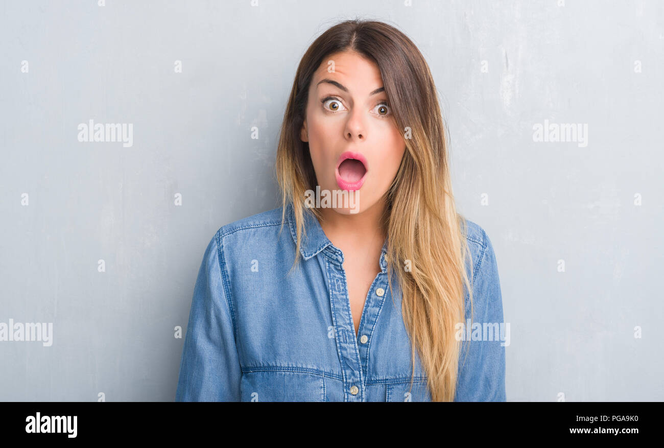 Young adult woman over grey grunge wall wearing denim outfit scared in ...