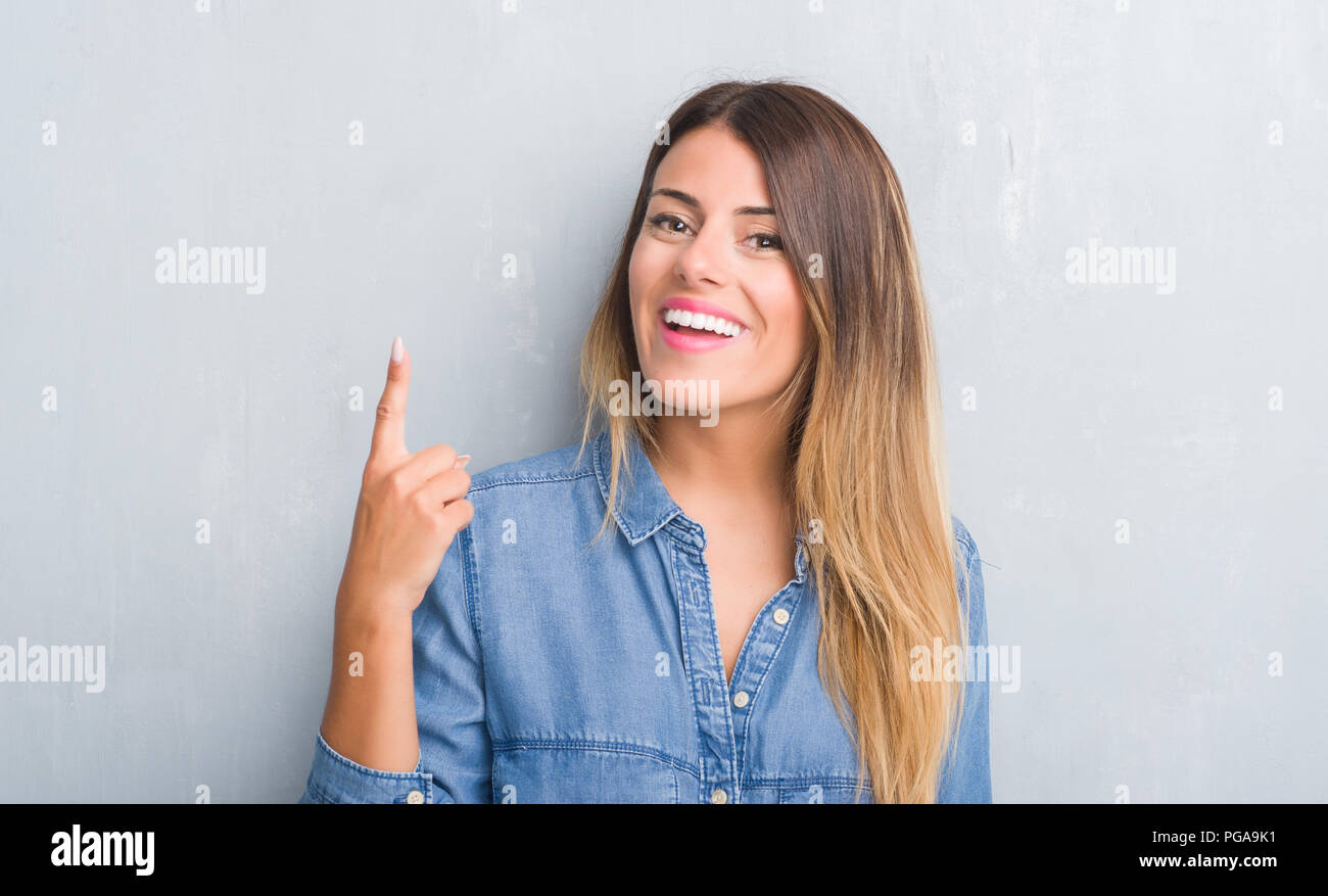 Young adult woman over grey grunge wall wearing denim outfit surprised ...