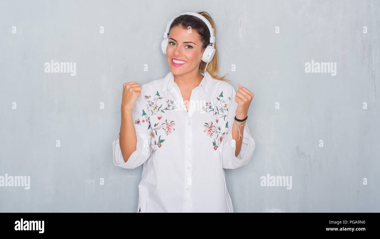 Young adult woman over grey grunge wall listening to music and dancing ...