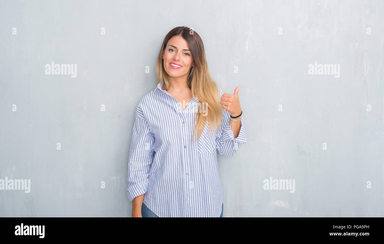 Young adult woman over grey grunge wall wearing fashion business outfit ...