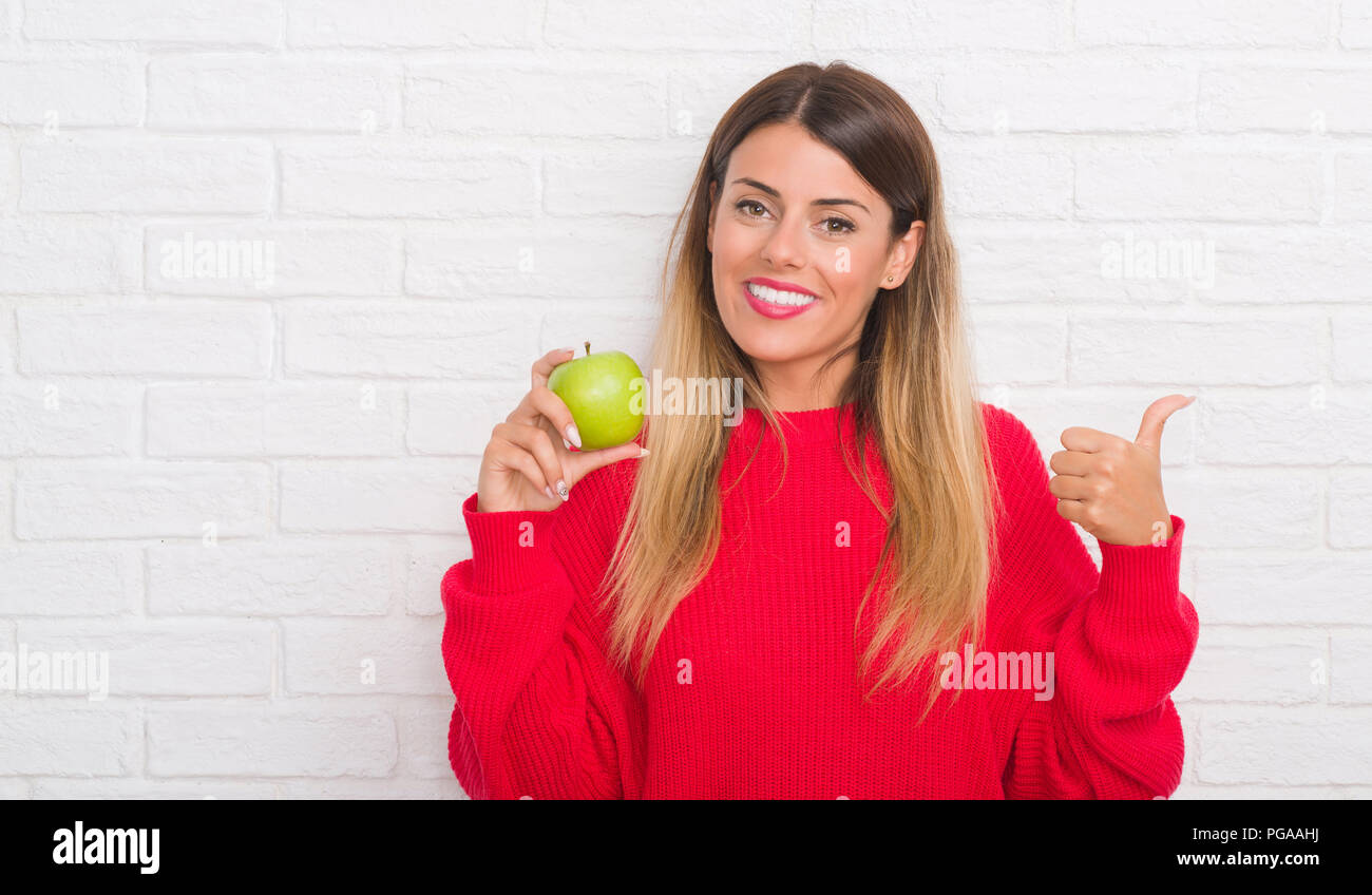 Young adult woman over white brick wall eating fresh green apple ...