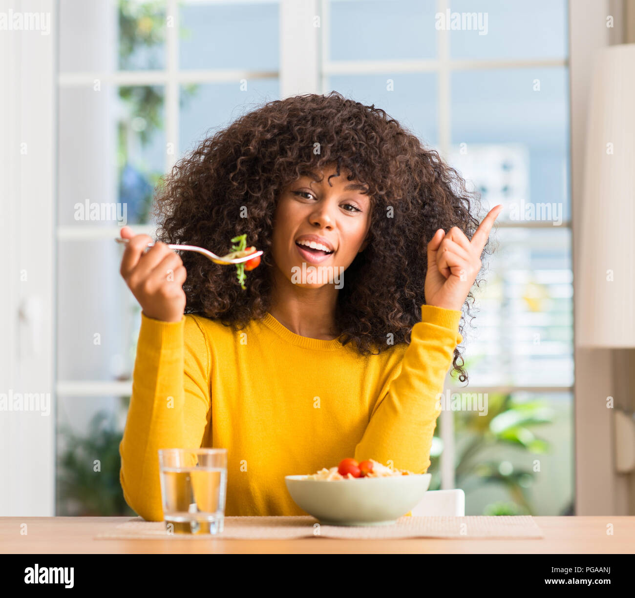 African american woman eating pasta salad at home surprised with an ...