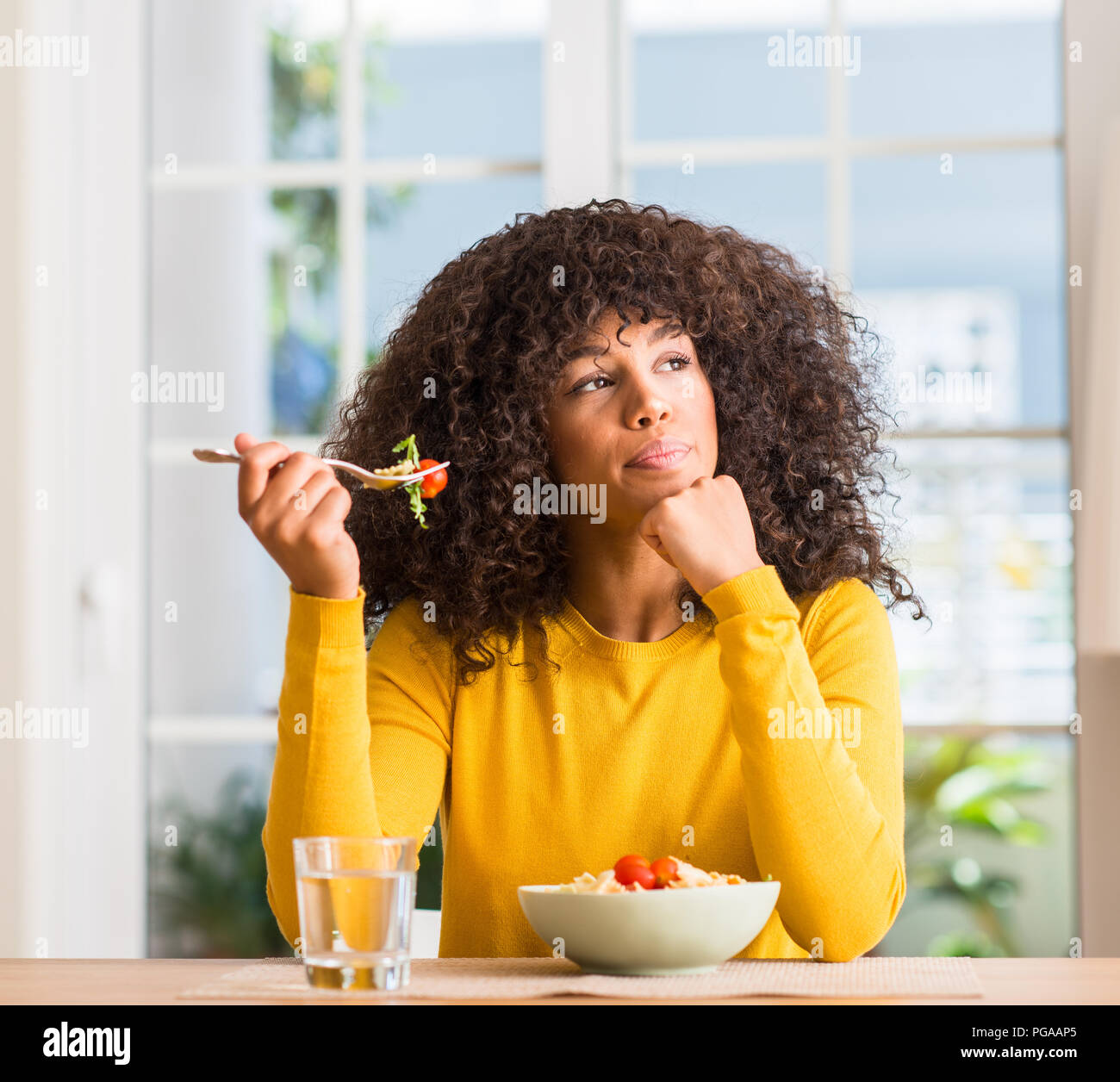 African american woman eating pasta salad at home serious face thinking ...