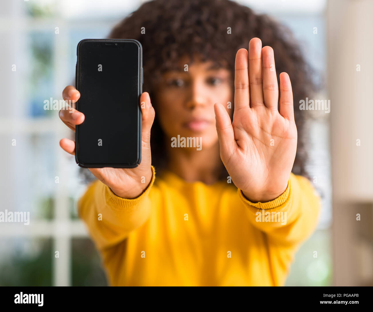 African american woman using smartphone with open hand doing stop sign ...