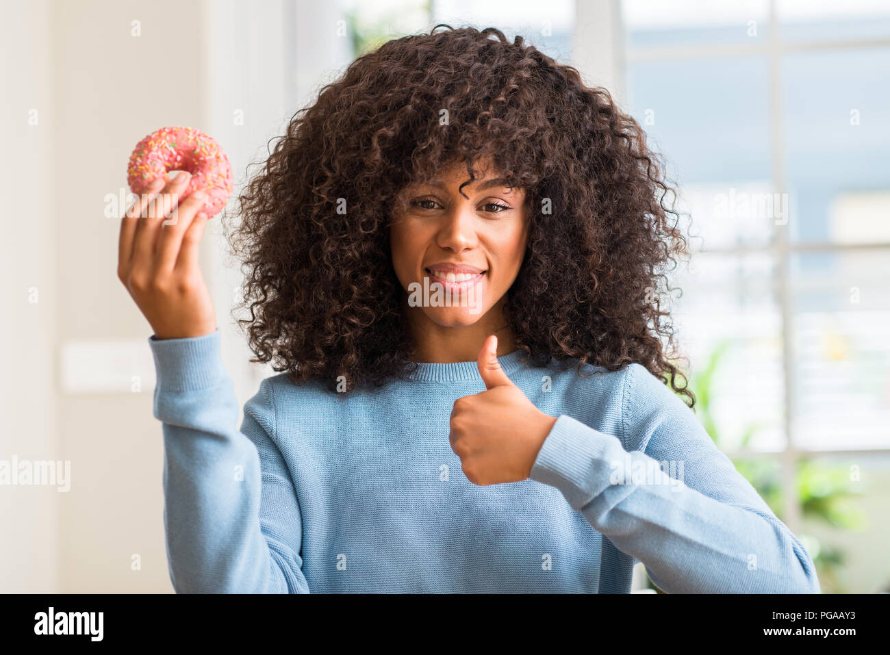 African american woman holding donut at home happy with big smile doing ...