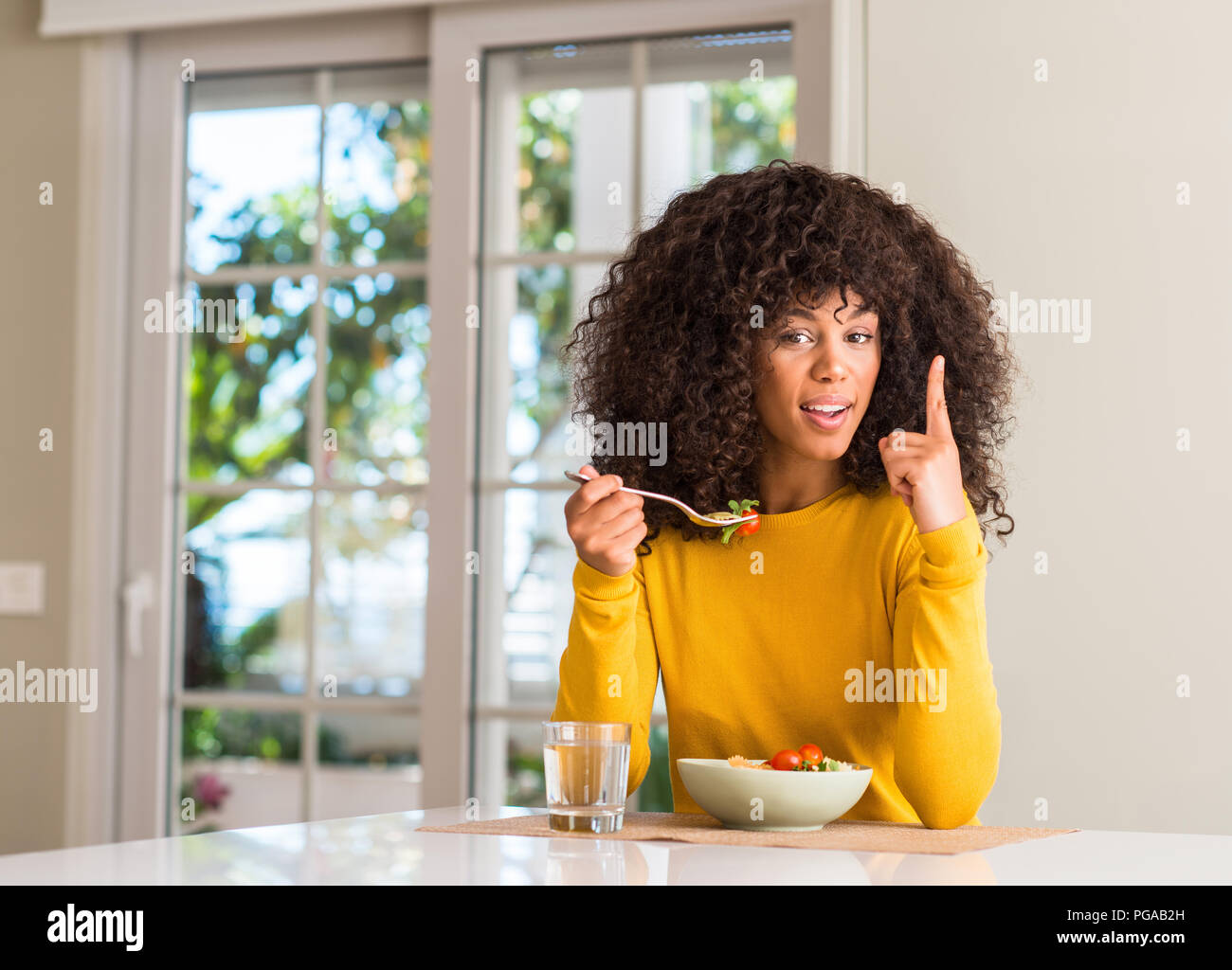 African american woman eating pasta salad surprised with an idea or ...
