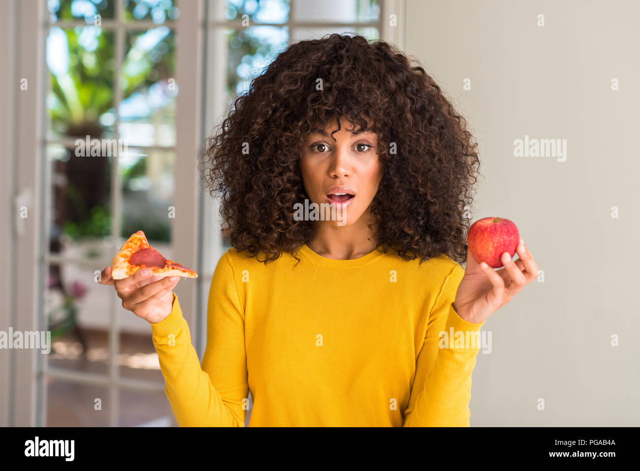 African american woman choosing between apple and pizza slice scared in ...