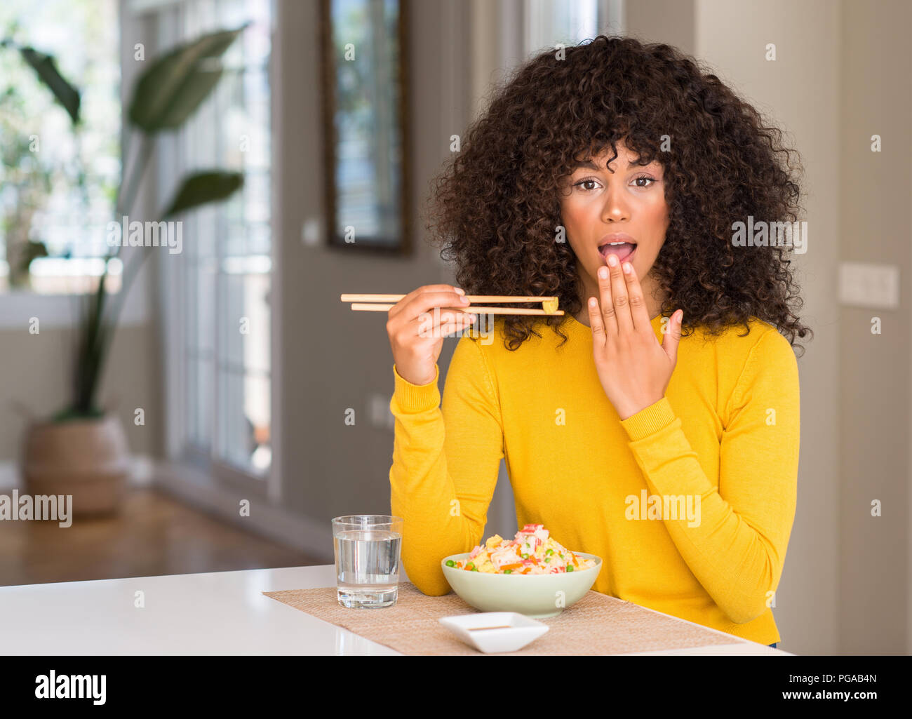 African american woman eating asian rice at home cover mouth with hand ...