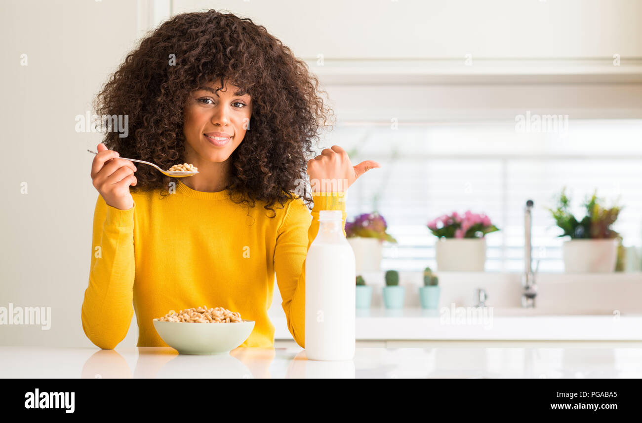 African american woman eating cereals and milk at home pointing with ...