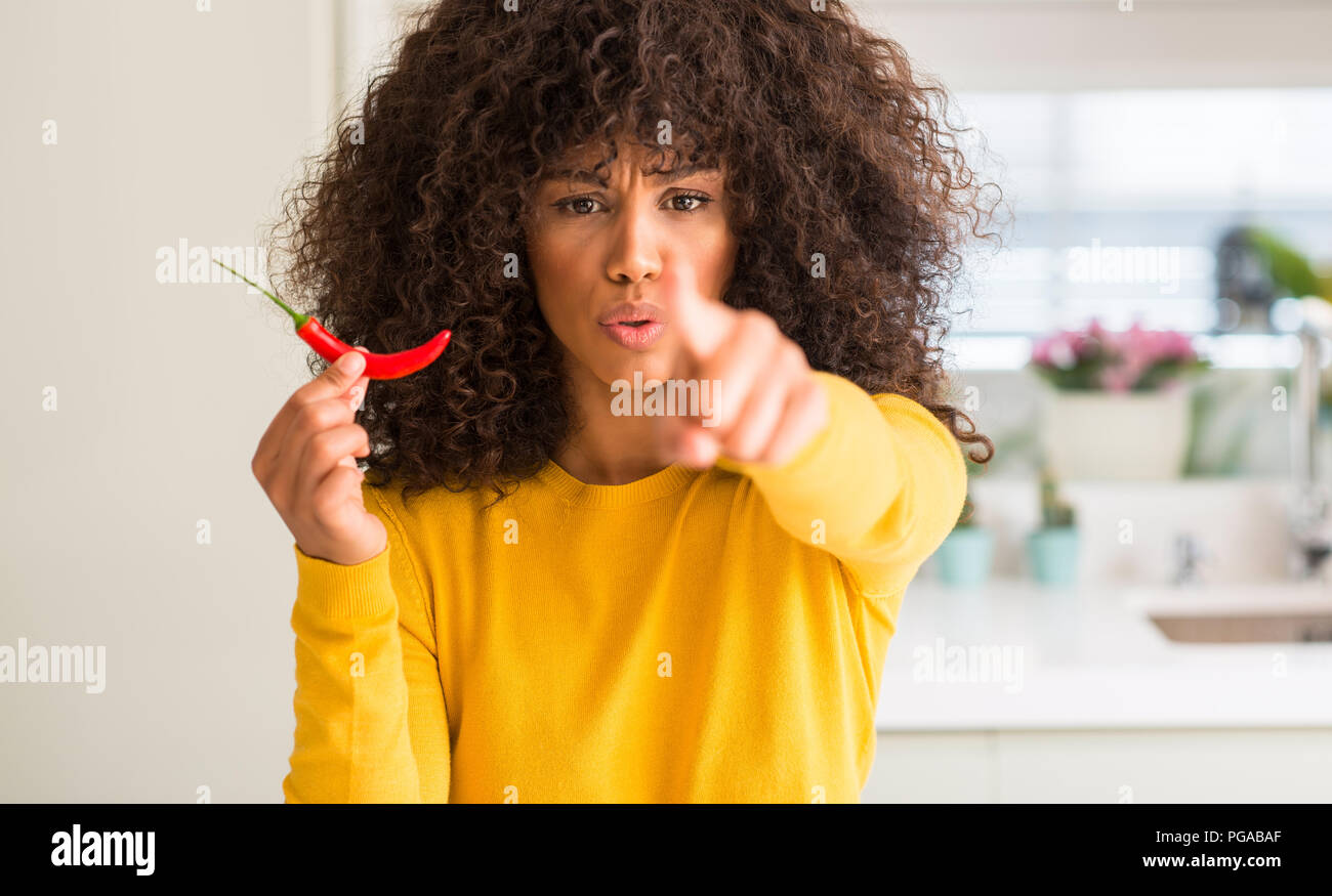 African american woman eating red hot chili pepper pointing with finger ...