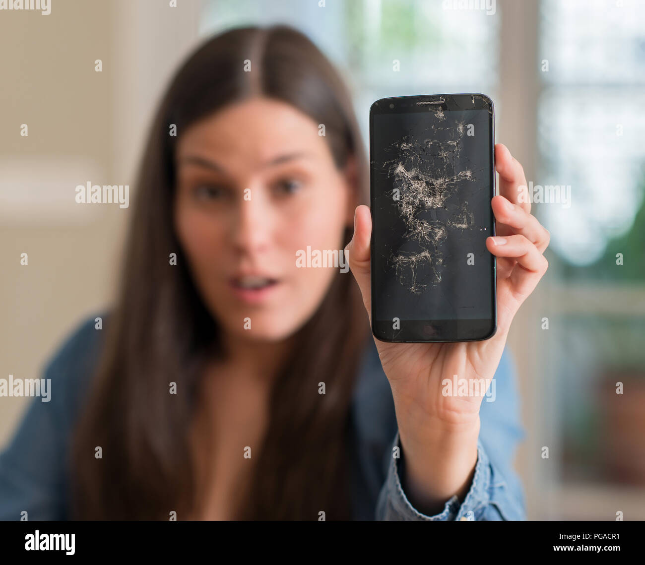 Brunette young woman holding broken smartphone scared in shock with a ...